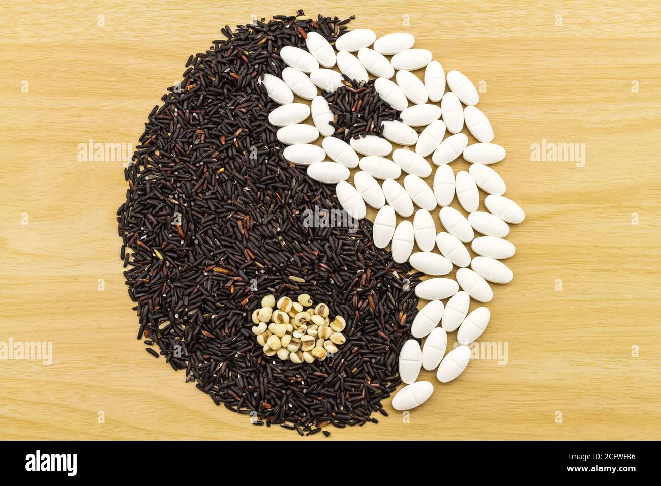 Black rice and white pill forming a yin yang symbol on brown wooden ...