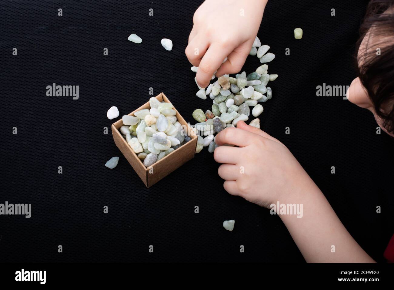 Hand filling the box with stone pebbles gravels on a black background ...