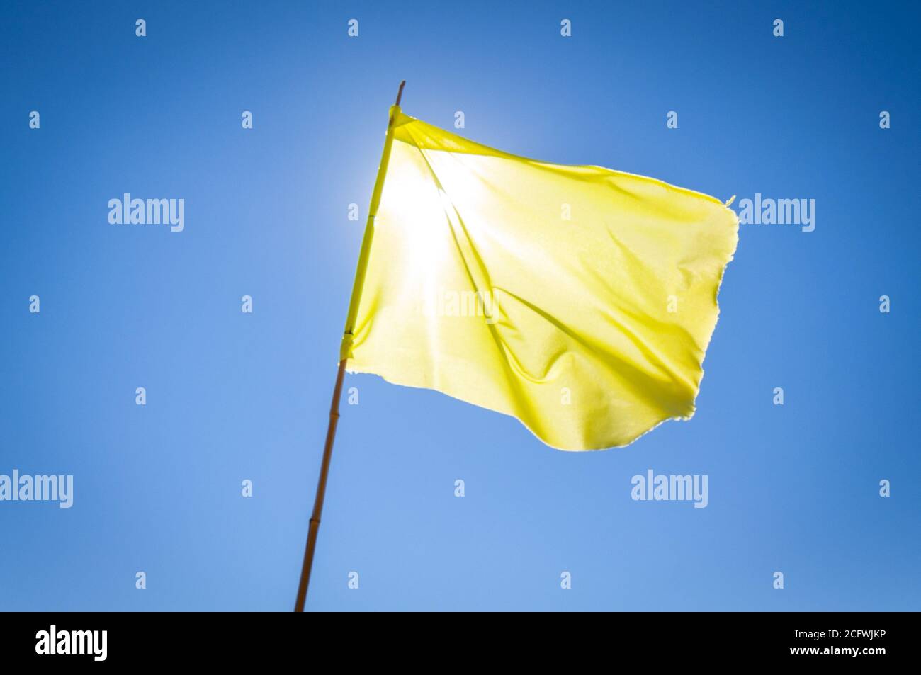 Yellow flag fluttering in deep blue sky in between the bright sun and ...