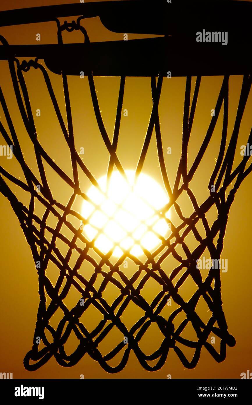 The sun sets frames by a silhouette of a basketball hoop making the ...