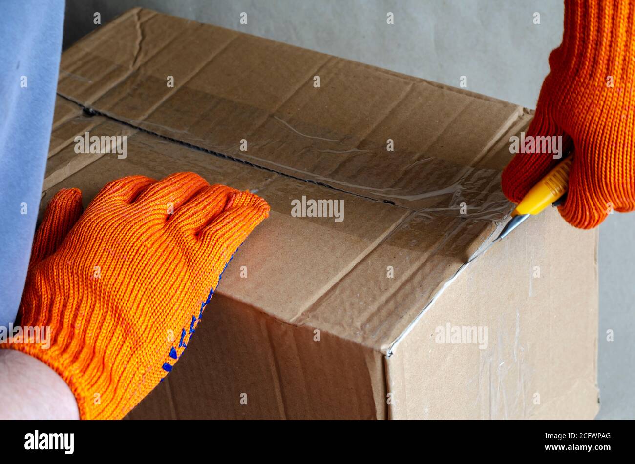 A worker wearing protective gloves opens a cardboard box. A hand with a ...