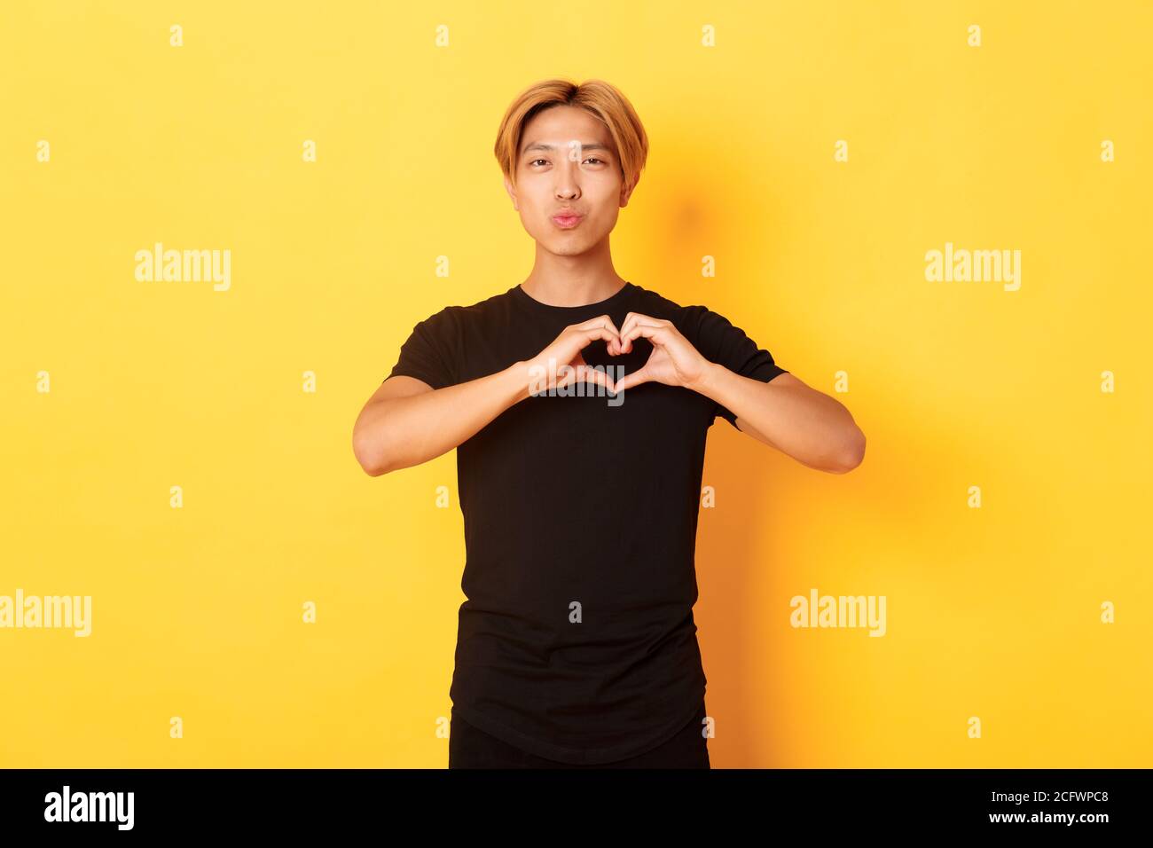 Portrait of lovely handsome blond asian man, showing heart gesture and ...