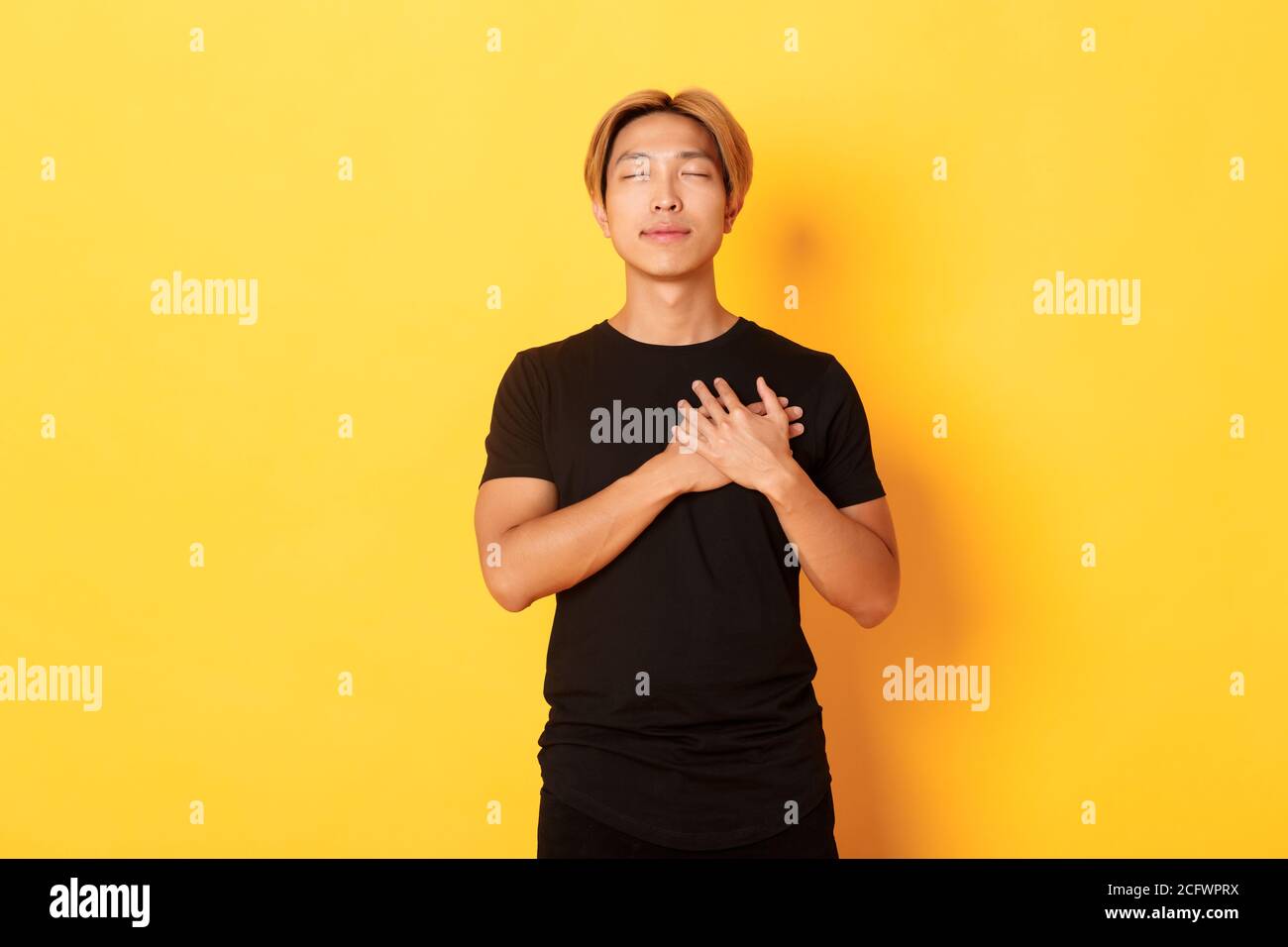 Portrait of touched handsome asian guy holding hands on heart and ...