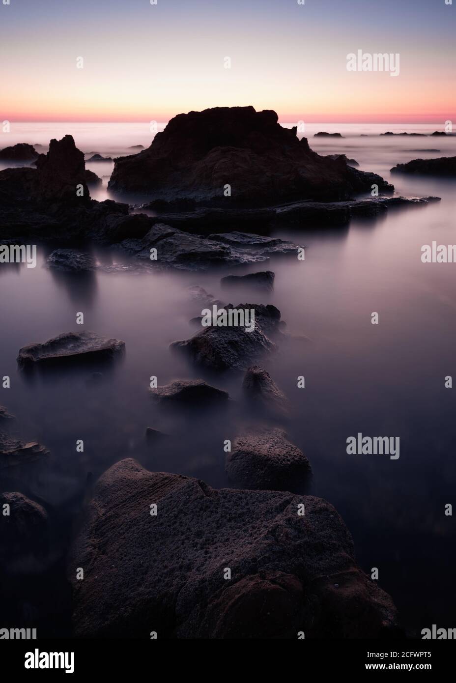 A path of rocks in the ocean leading to a larger rock during dusk with ...