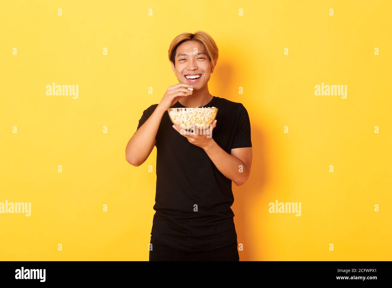 Carefree happy asian guy with blond hair, watching comedy, laughing and ...