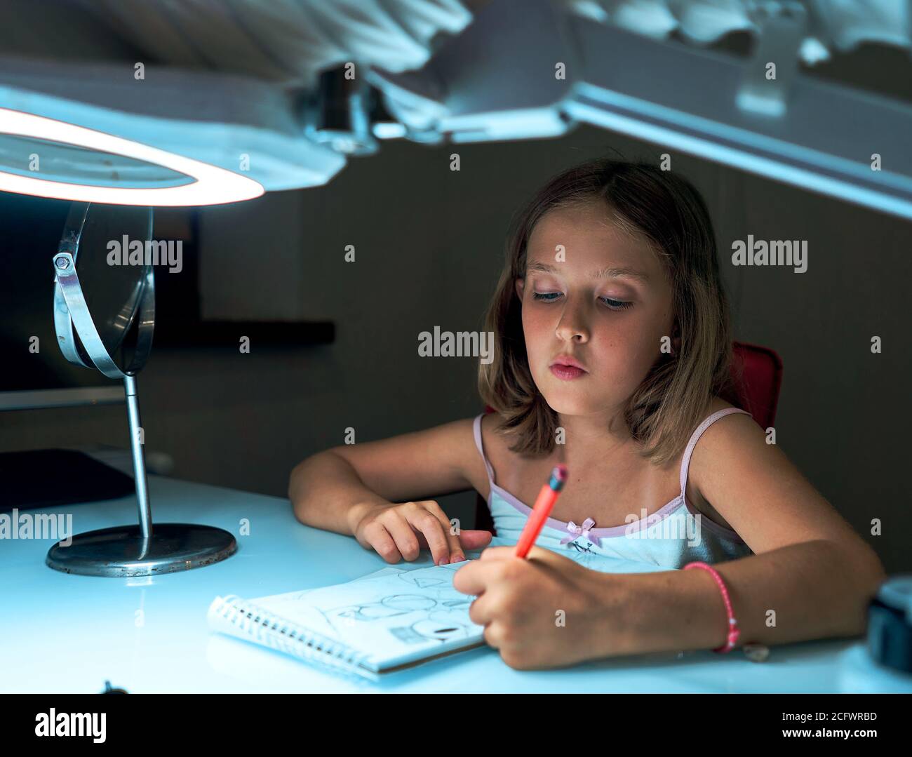 Smiling Asian schoolgirl doing homework while sitting at the desk at ...