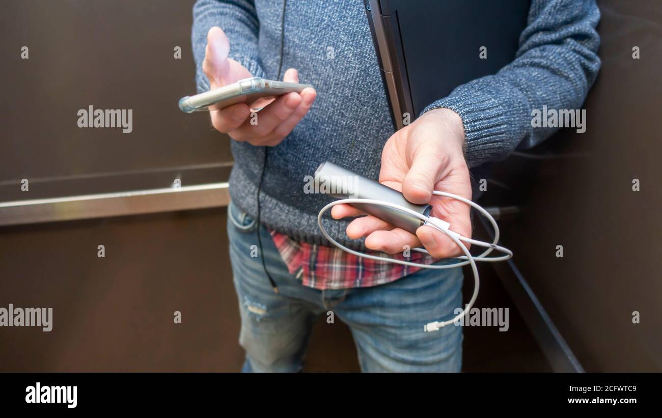 cell phone and poarbale battery charger in man's hands in an elevator ...