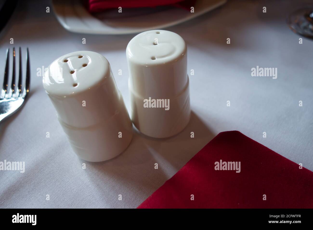 ceramic white spice shakers sitting on white cloth table with with red ...