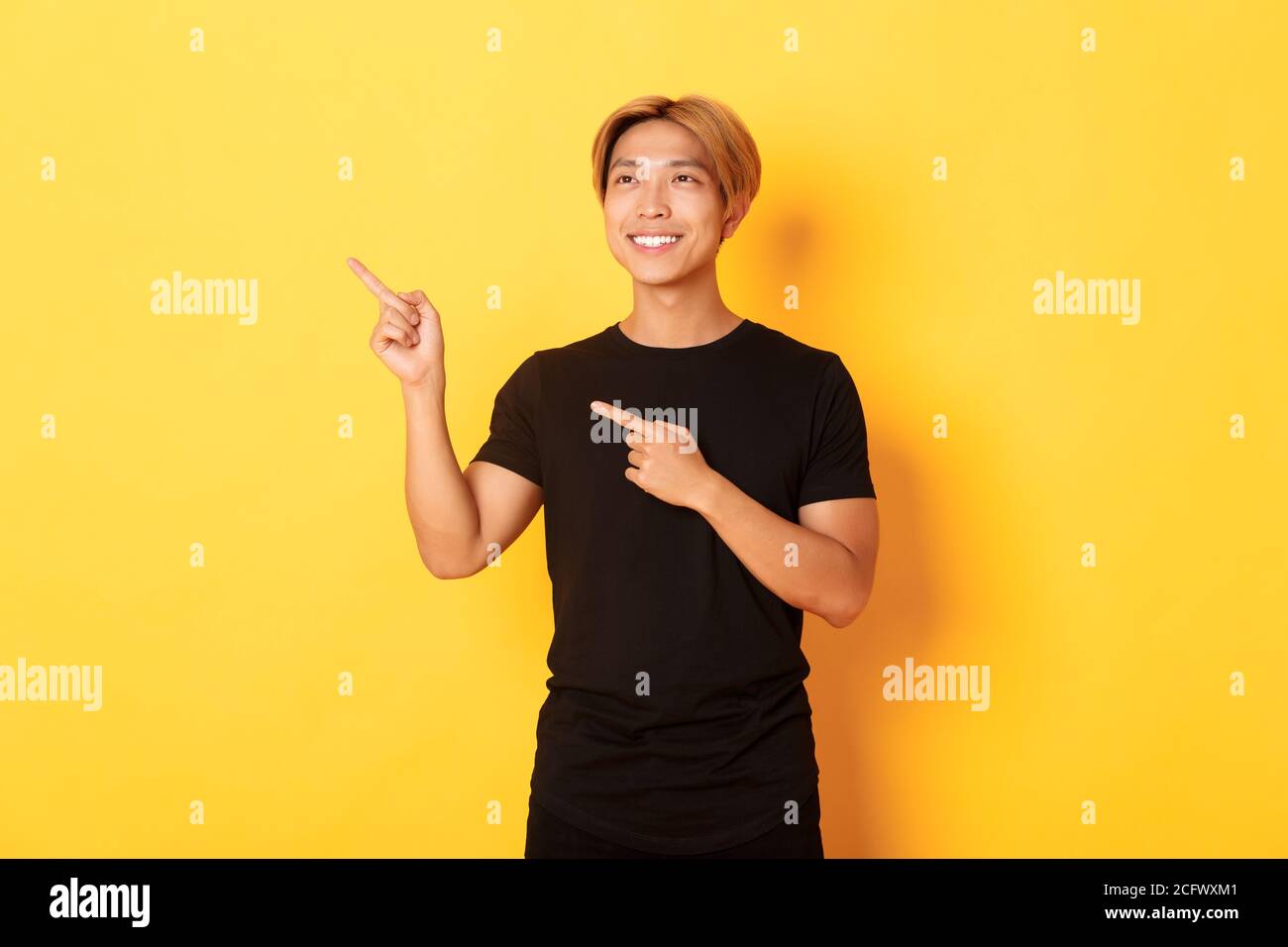 Portrait of handsome korean blond guy, pointing fingers upper left ...