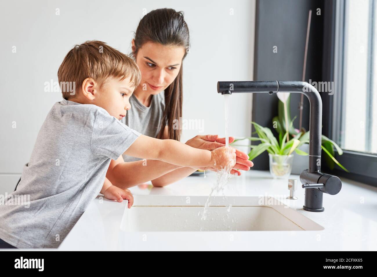 Child learns hand washing with soap by mother by the sink at home Stock ...