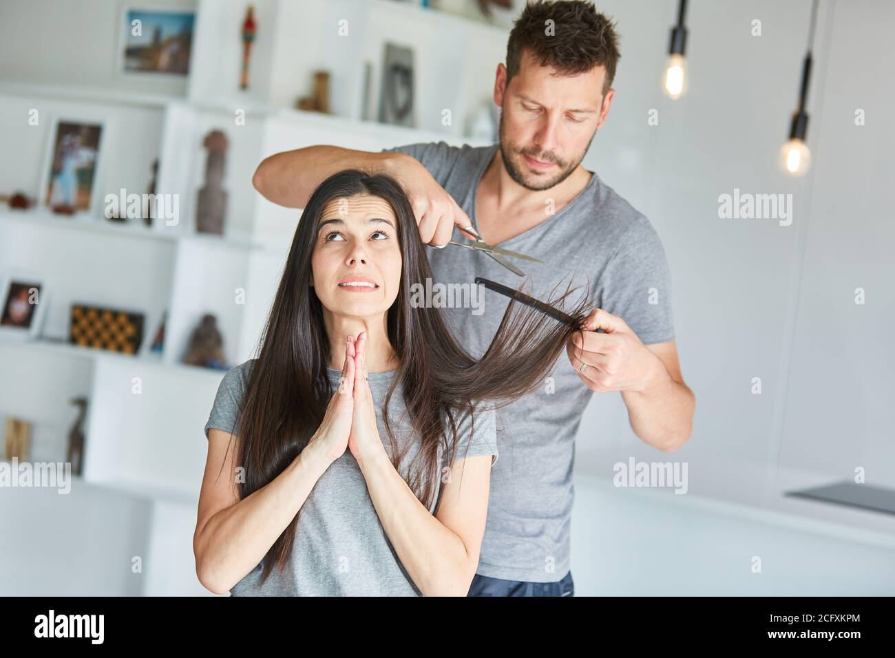Afraid woman folds her hands while cutting hair as DIY by her husband ...