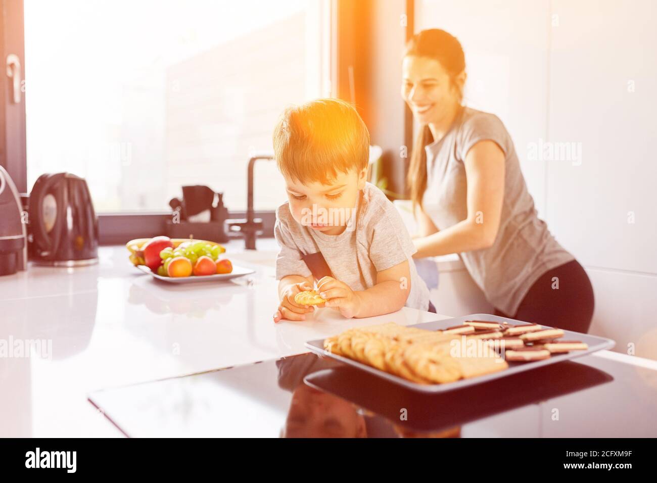 Little child eating biscuit in kitchen with laughing mother in the ...