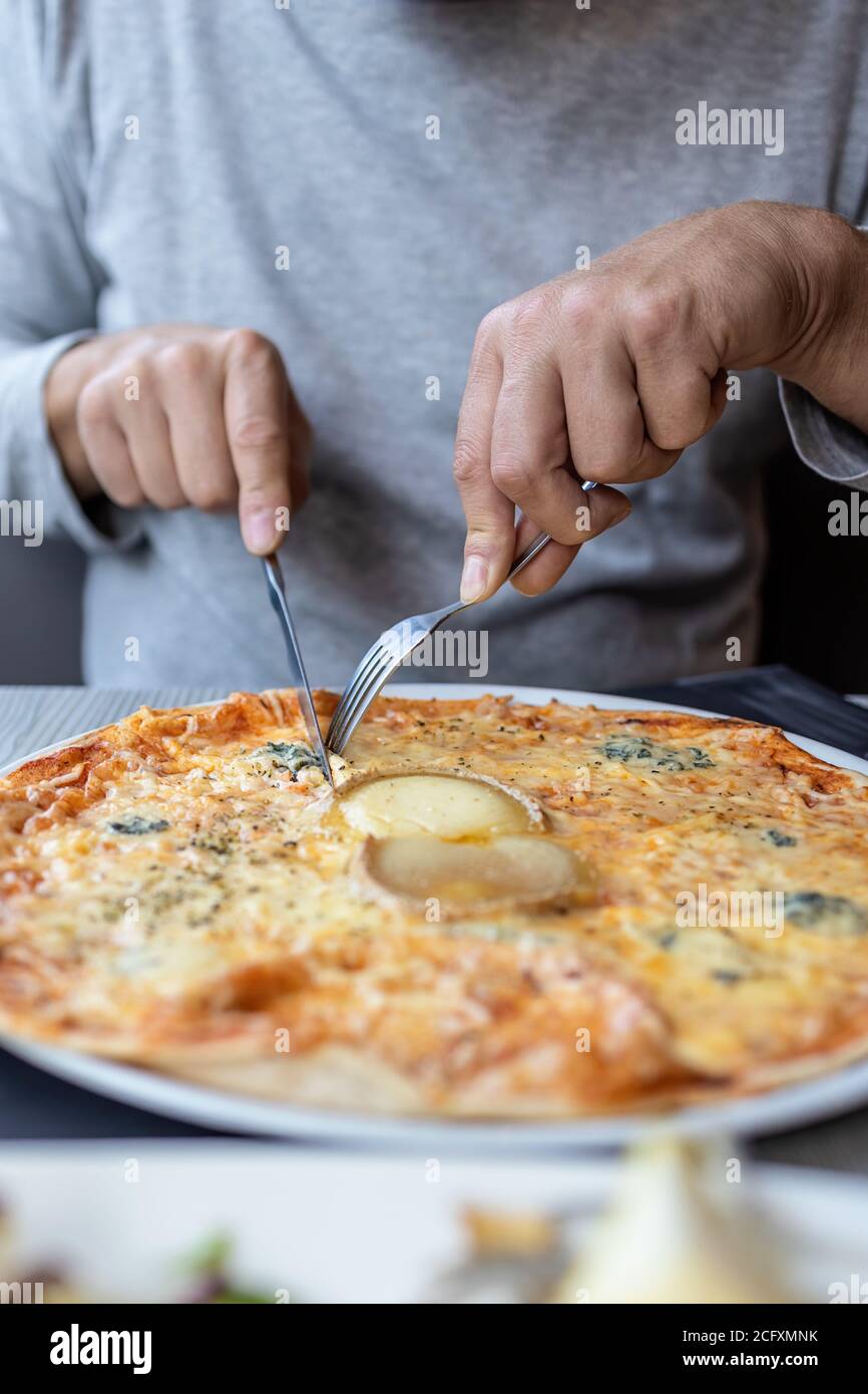 Man eating delicious cheesy pizza in the restaurant with fork and knife ...