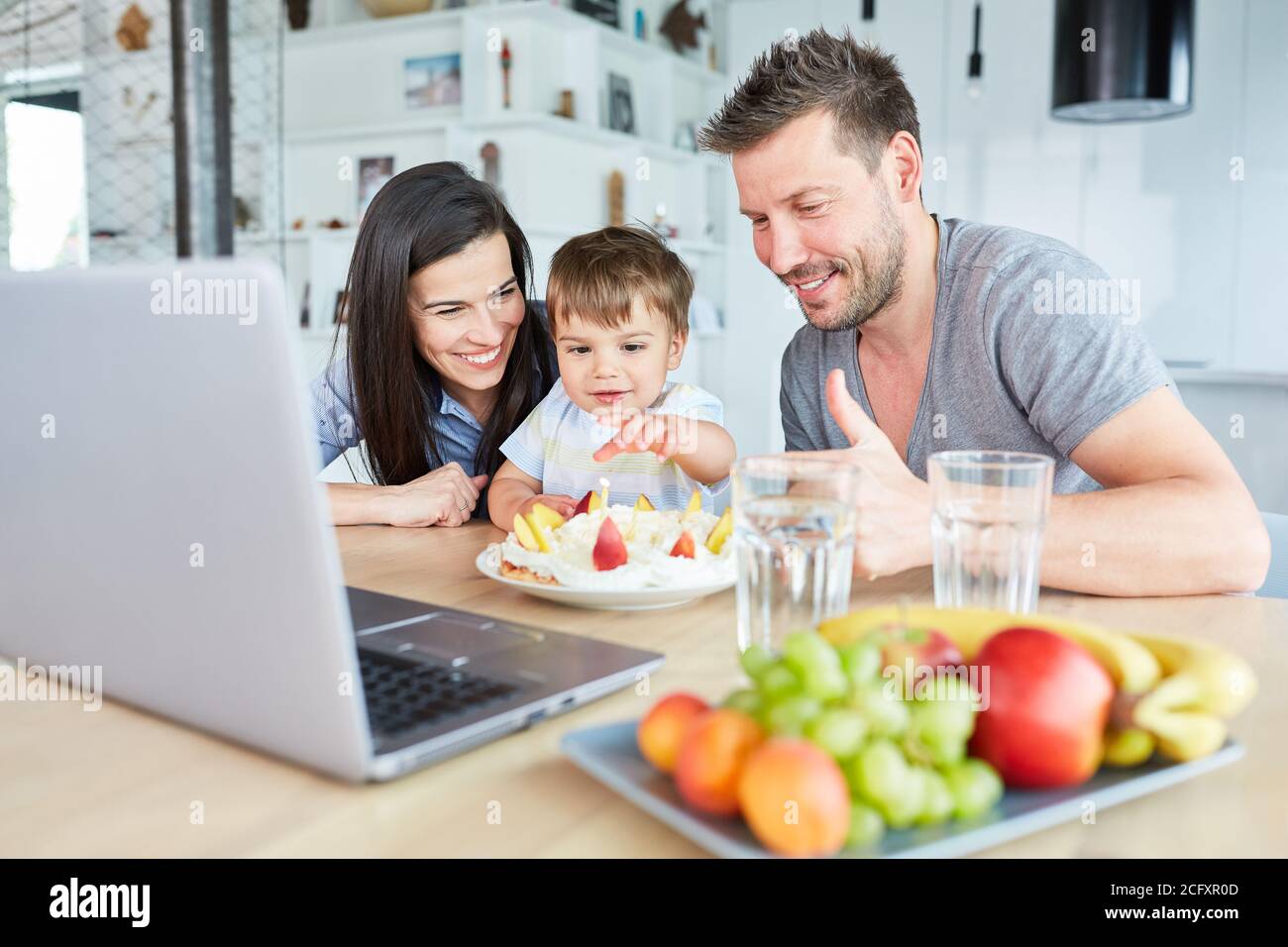 Parents and child eat cake for birthday while video chat on laptop ...
