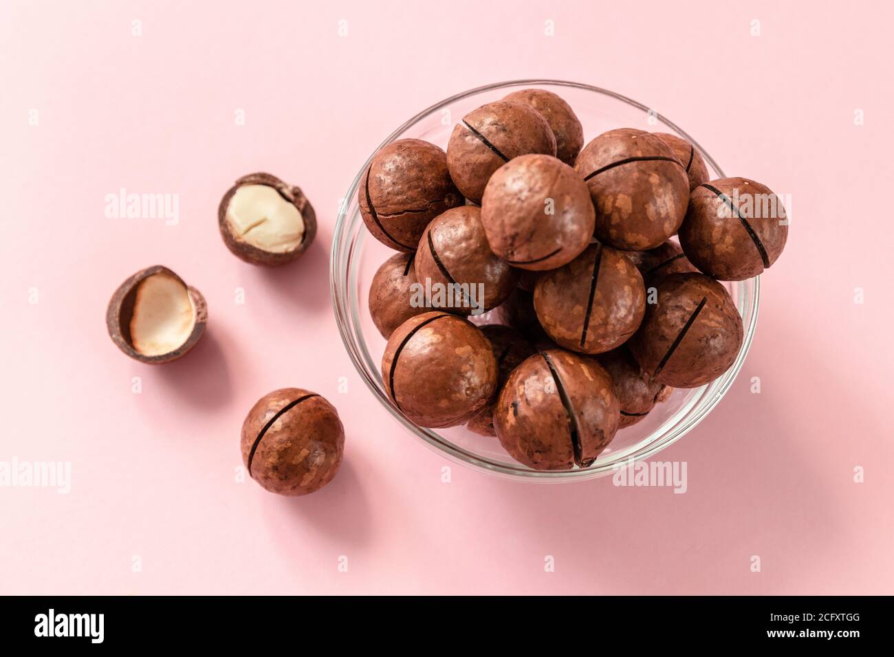 Raw macadamia nuts in a transparent glass bowl and scattered on pink ...
