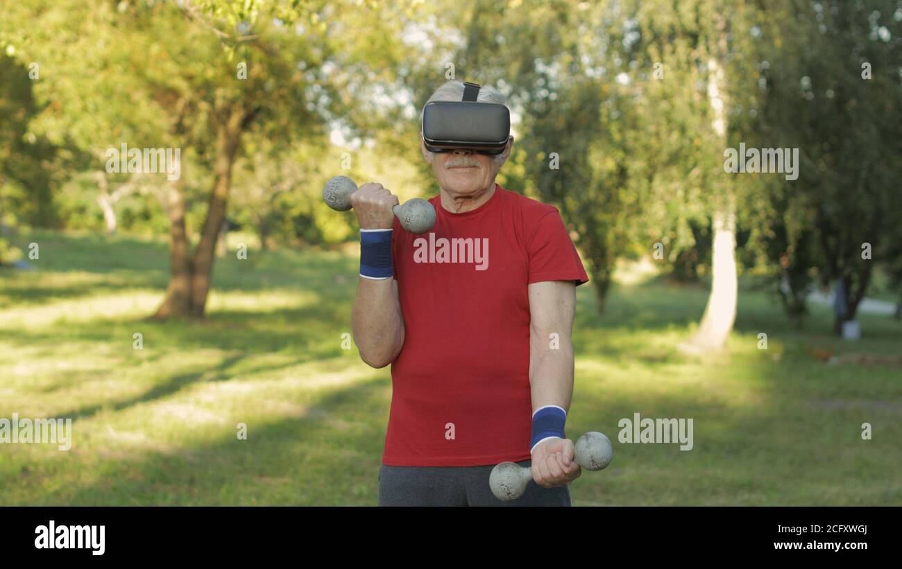 Elderly man in VR headset helmet making fitness exercises with ...