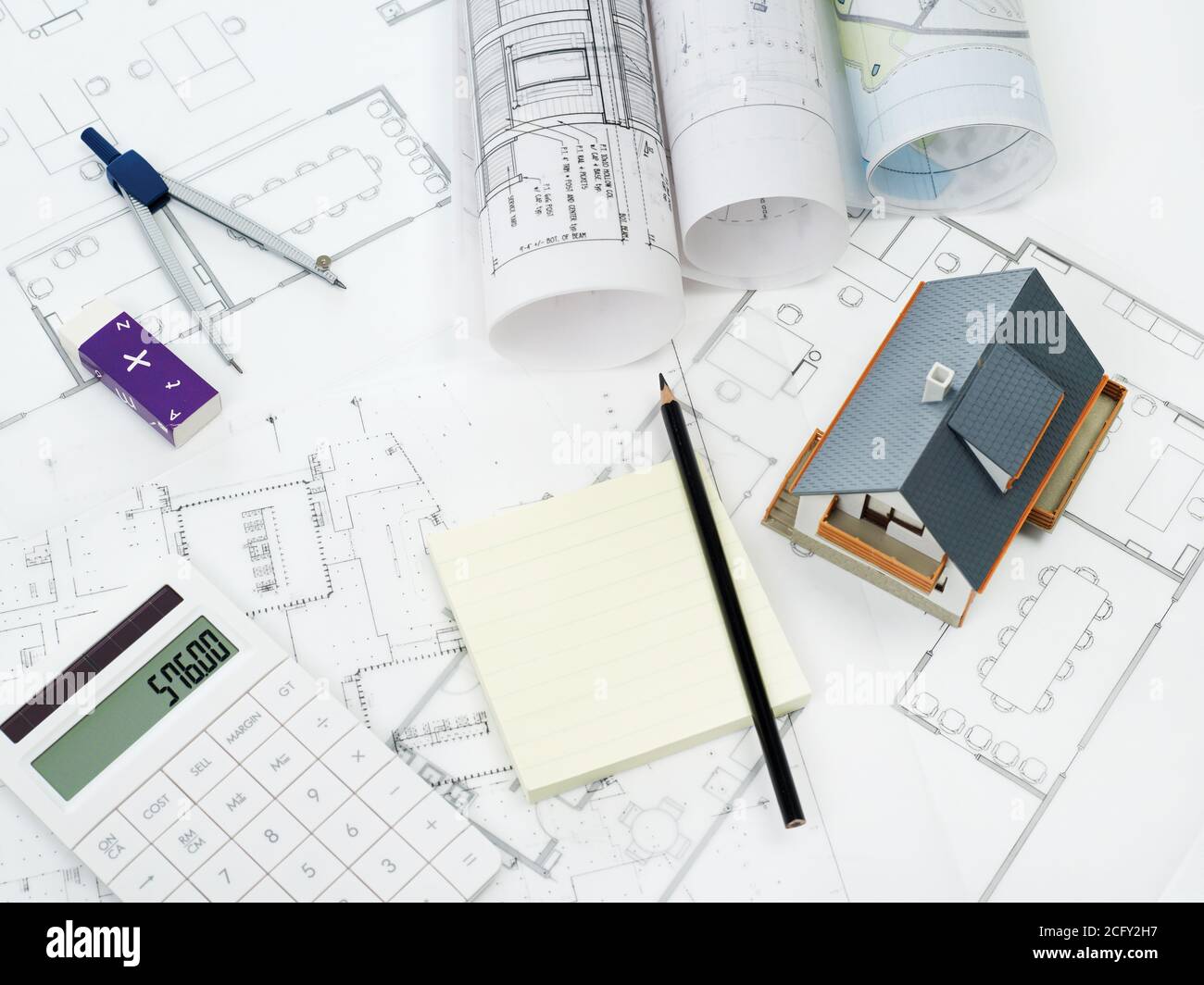 Model house, postit, drawing compass and calculatoron top of blueprints ...