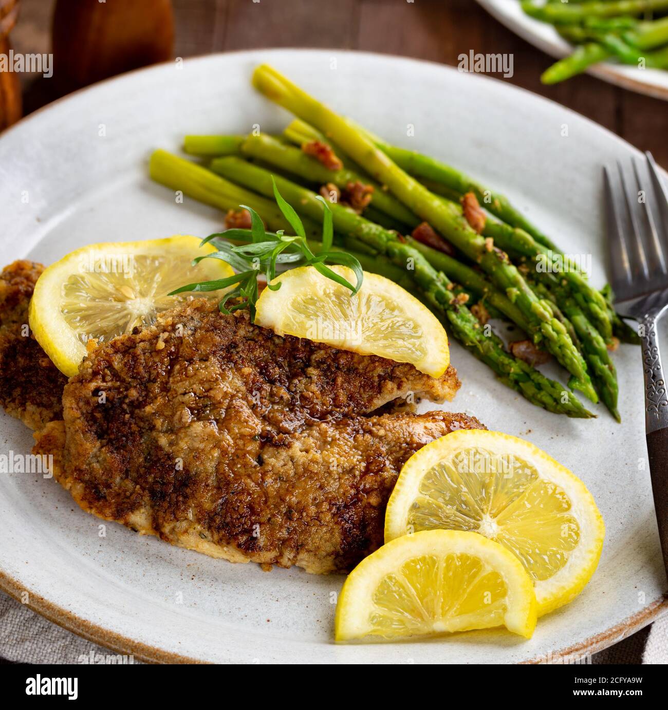 Baked tilapia fish fillets with sliced lemons and asparagus on a dinner ...