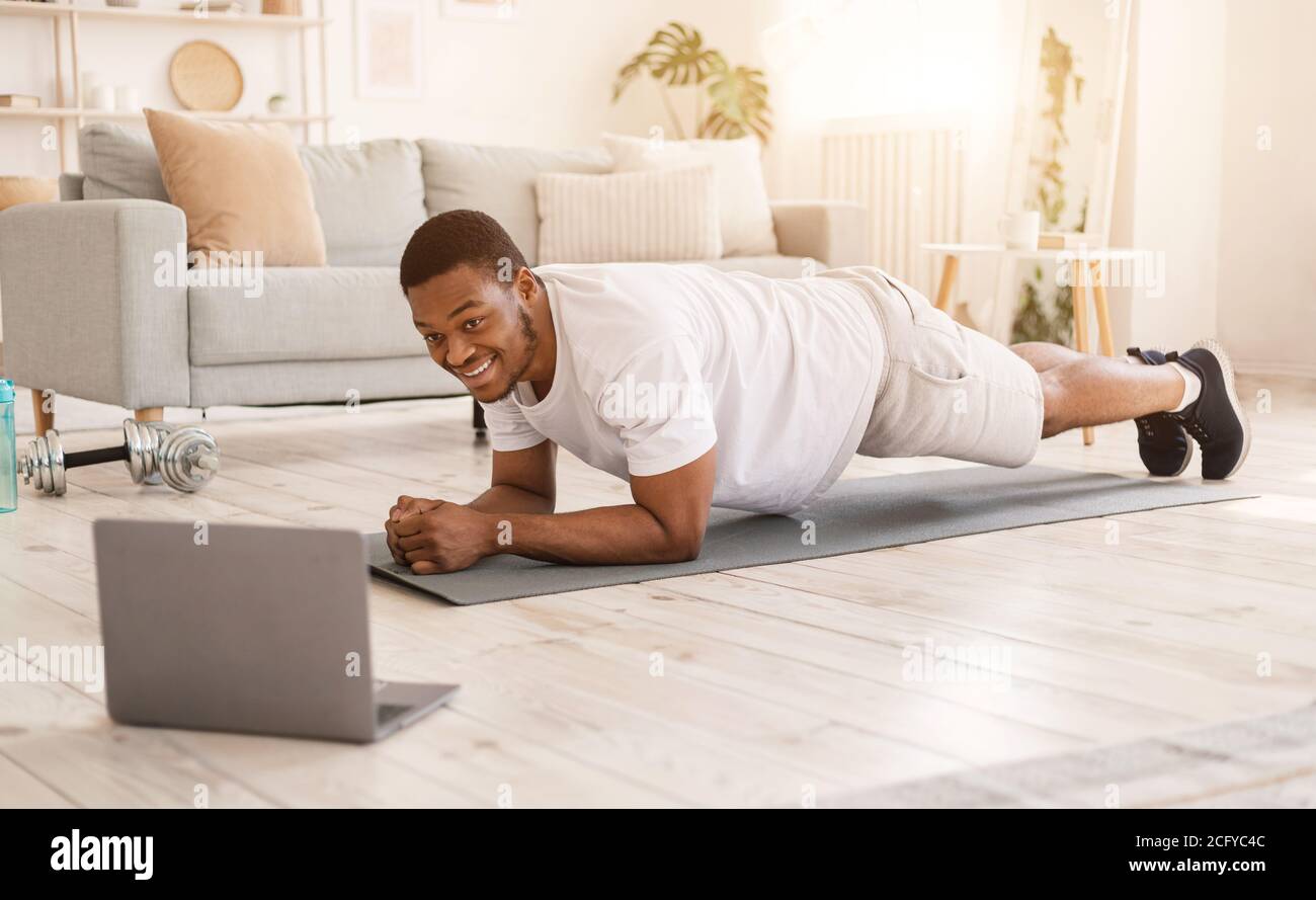 African Guy Training At Laptop Doing Plank Exercise In Bedroom Stock ...