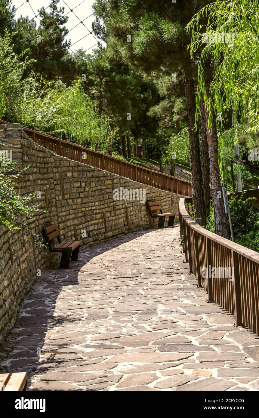Paved path covered with rough stone, with benches against a stone wall ...