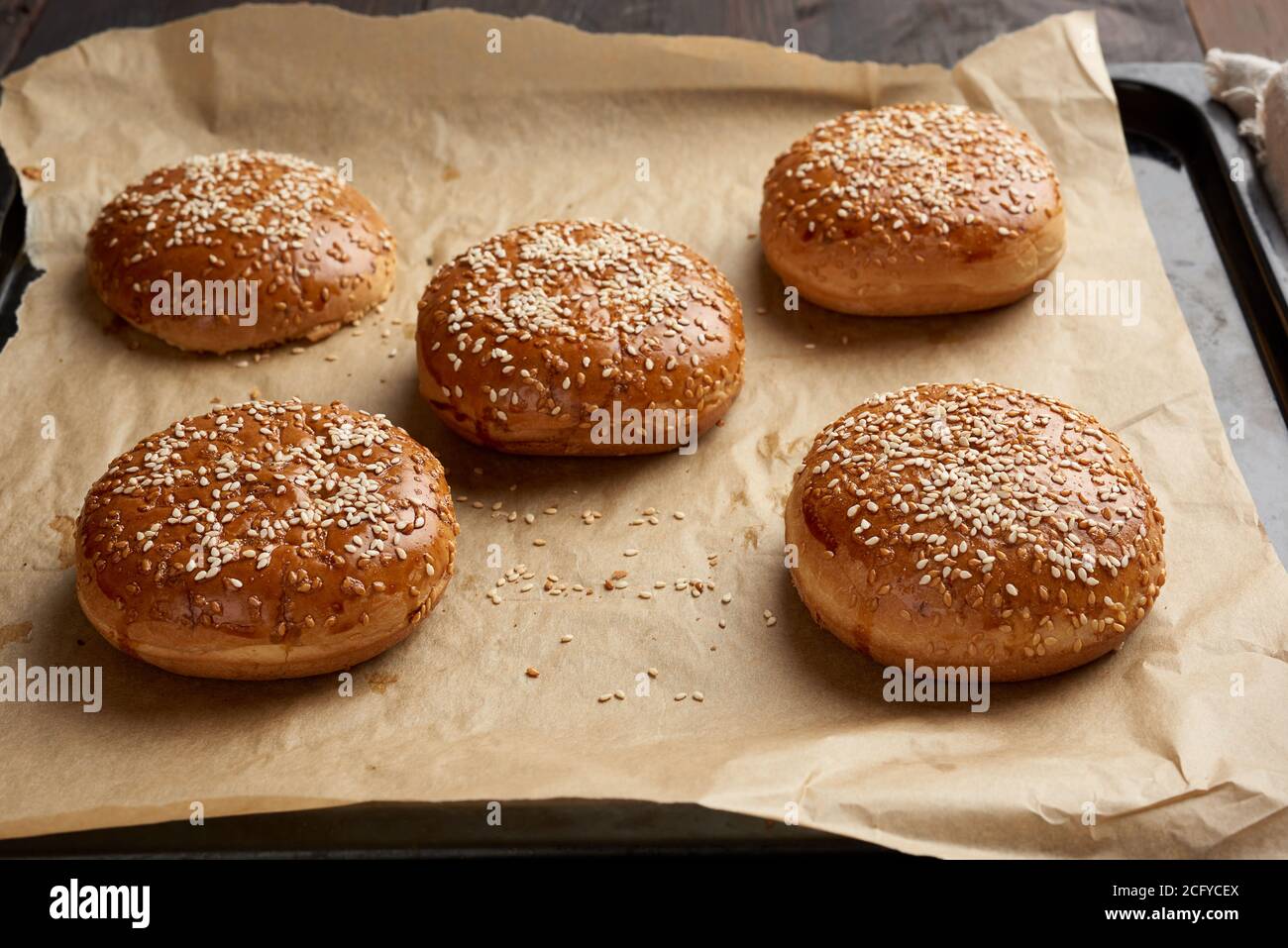 baked sesame buns on brown parchment paper, ingredient for a hamburger ...