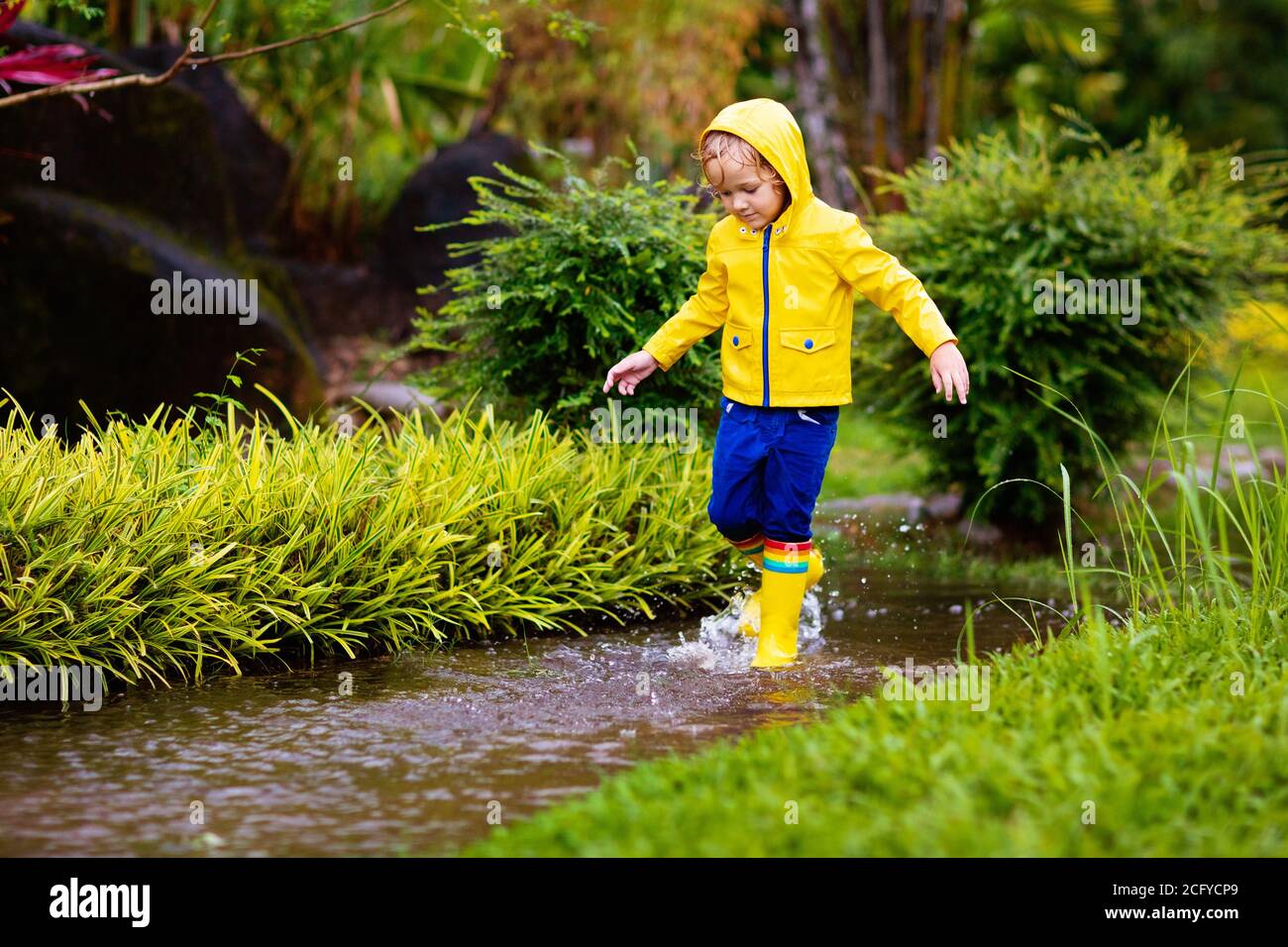 Kid playing in the rain in autumn park. Child jumping in muddy puddle ...