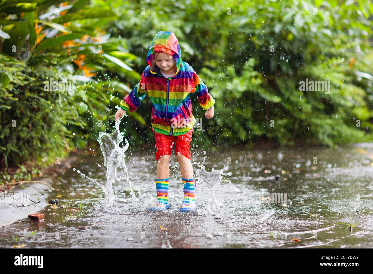 Kid playing in the rain in autumn park. Child jumping in muddy puddle ...