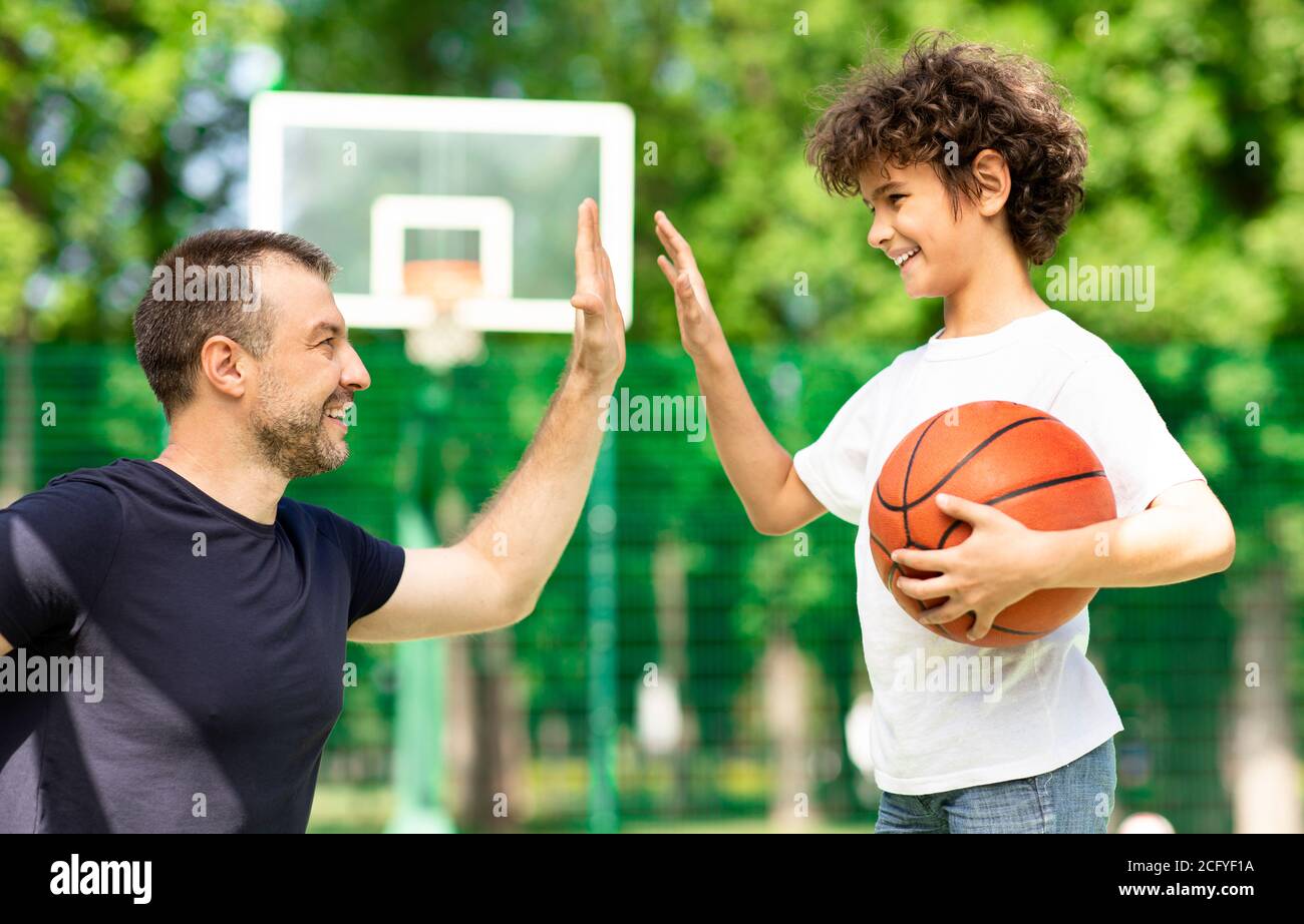 Portrait of man and boy giving high five playing basketball Stock Photo ...