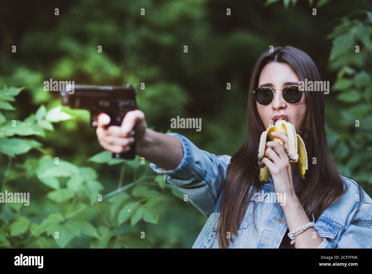 girl eats a banana and at the same time aims from a pistol Stock Photo ...