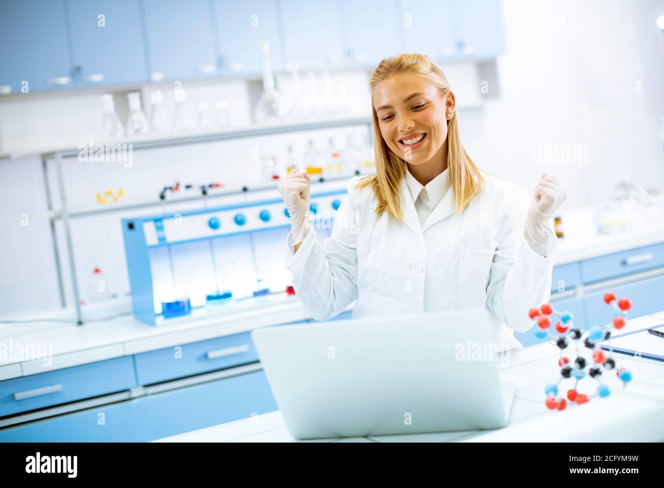 Cute happy female researcher in white lab coat using laptop while ...