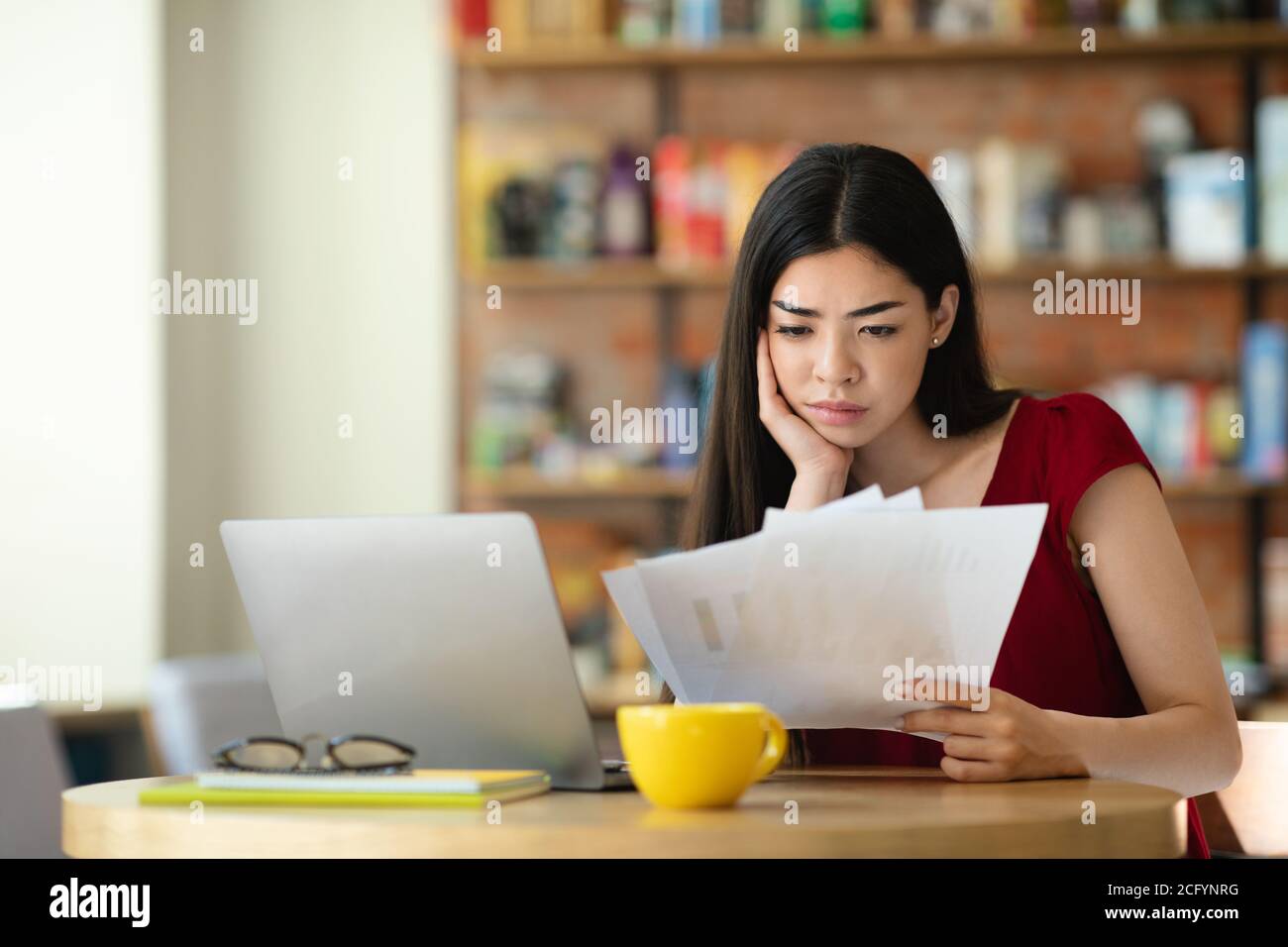 Concentrated female employee working with papers and laptop at cafe ...