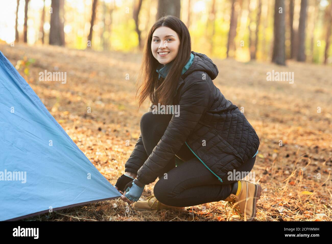 Cheerful woman setting up tent, forest background Stock Photo - Alamy