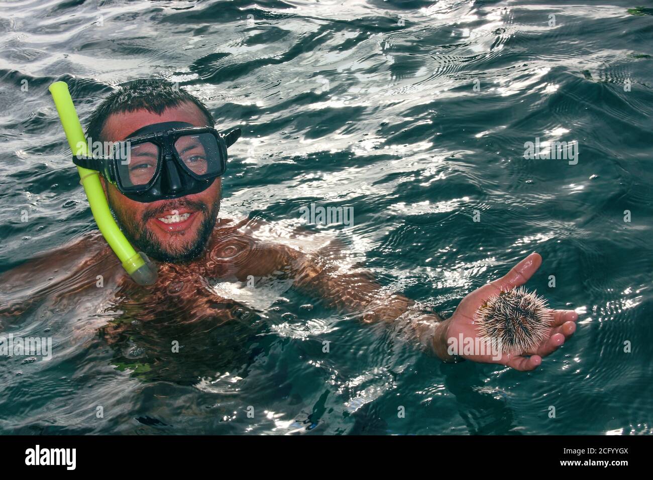 Smiling handsome young man in diving mask looks at camera and shows sea ...