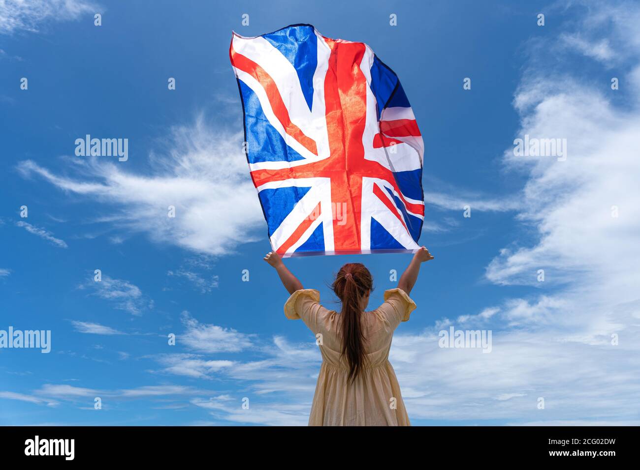 woman standing and holding UK flag under blue sky Stock Photo - Alamy