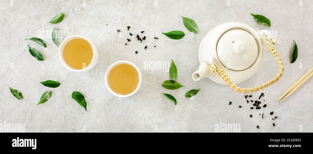 Herbal tea with two white tea cups and teapot, with green tea leaves ...