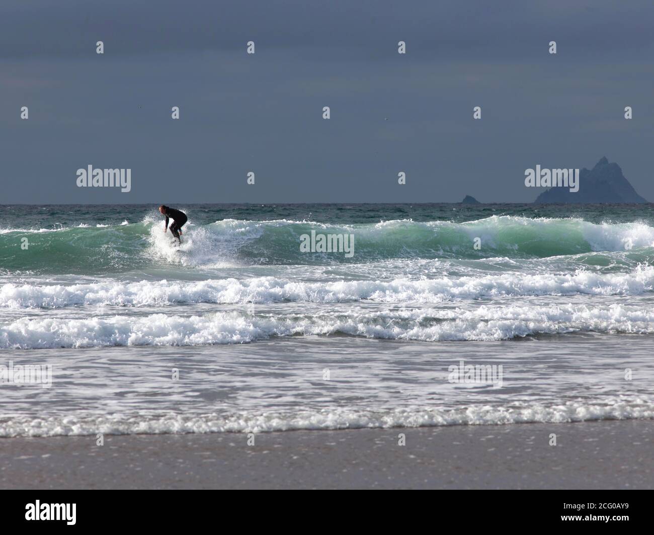 A surfer rides the waves with The Skellig Islands in the background at ...