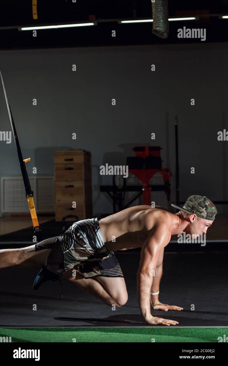 Muscular man exercising in health club. Using TRX bands, doing push-ups ...