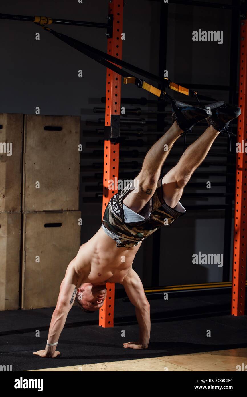 Muscular man exercising in health club. Using TRX bands, doing push-ups ...