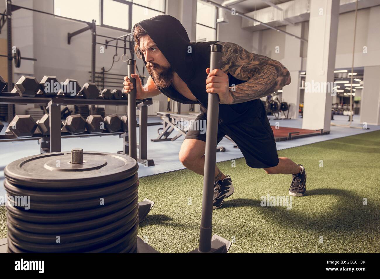 Muscular and strong young man pushing the exercise equipment at the gym ...