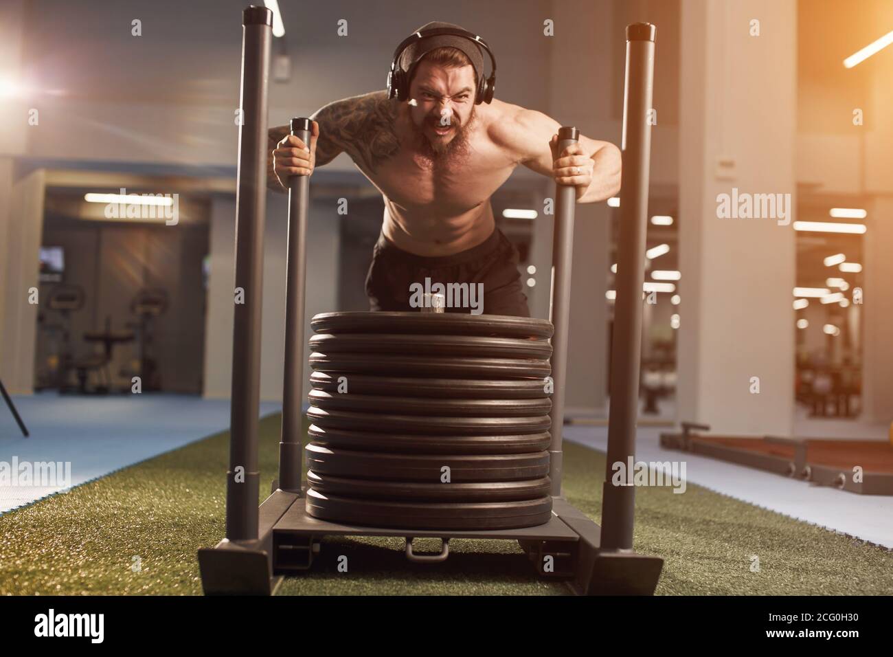 Muscular and strong young man pushing the exercise equipment at the gym ...