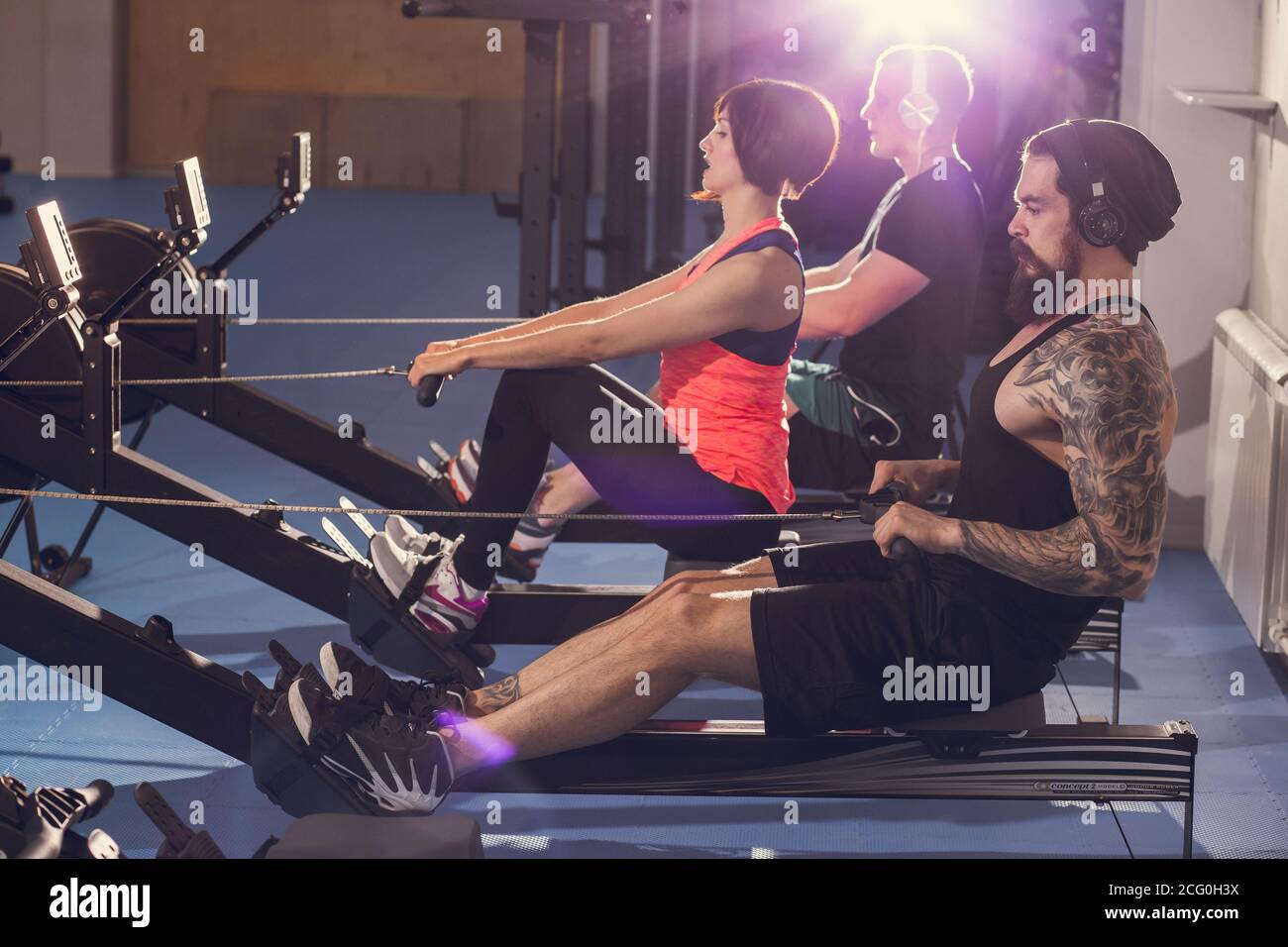 Happy friends training on rowing machine in gym Stock Photo - Alamy
