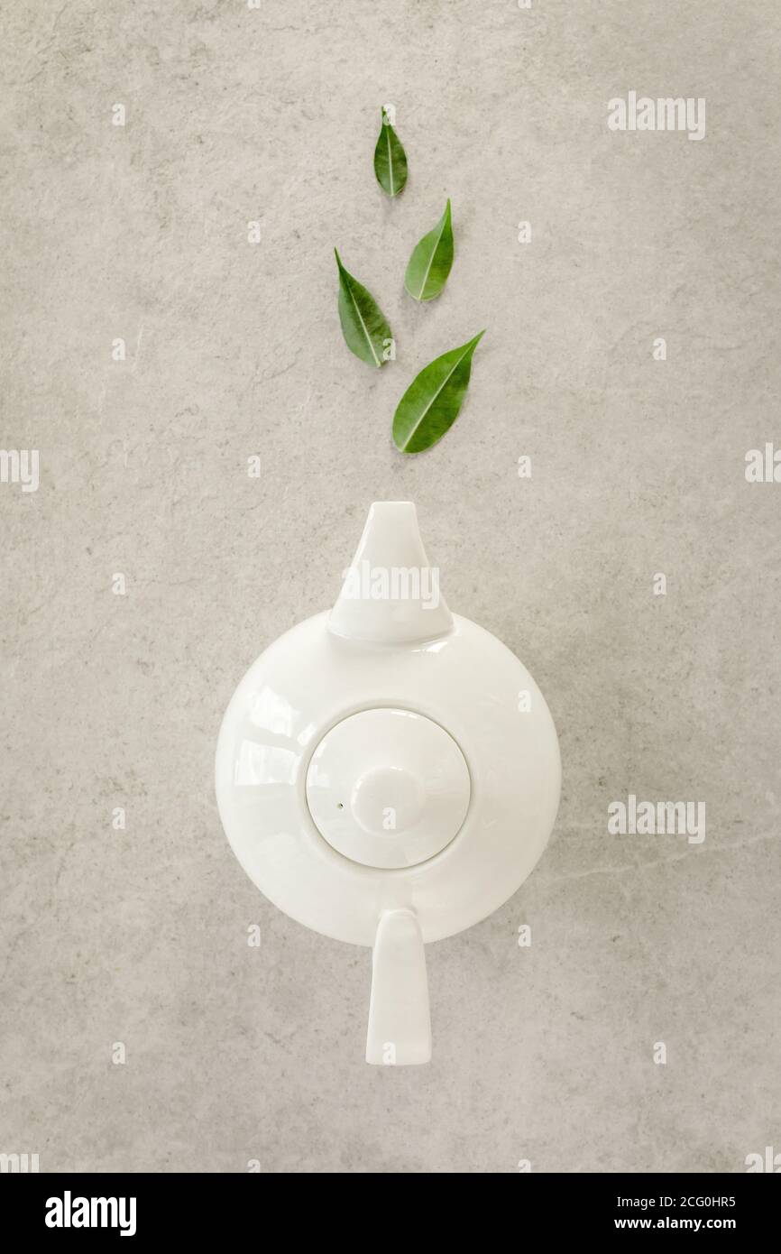 Herbal tea in a white teapot, with green tea leaves. Flat lay, top view ...