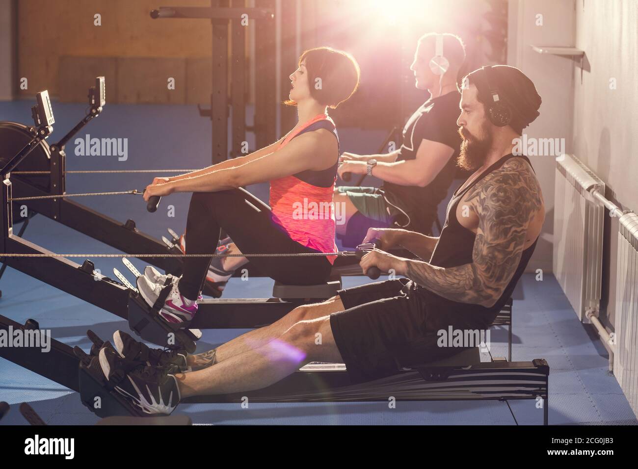 Side view of man and woman doing exercises with rowing machine at gym ...