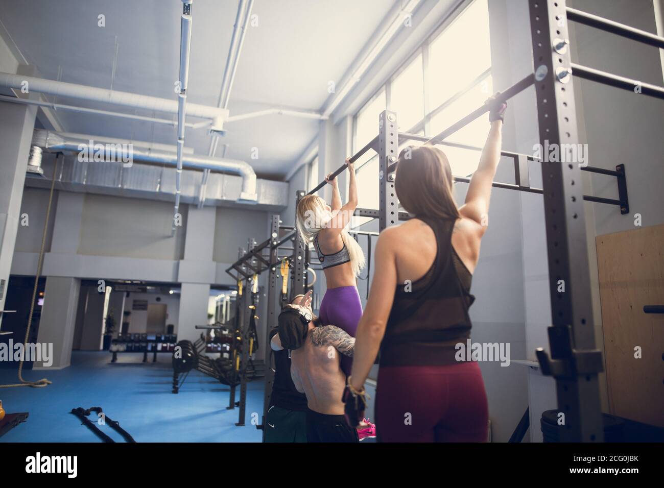 Group of attractive young male and female adults doing pull ups on bar ...