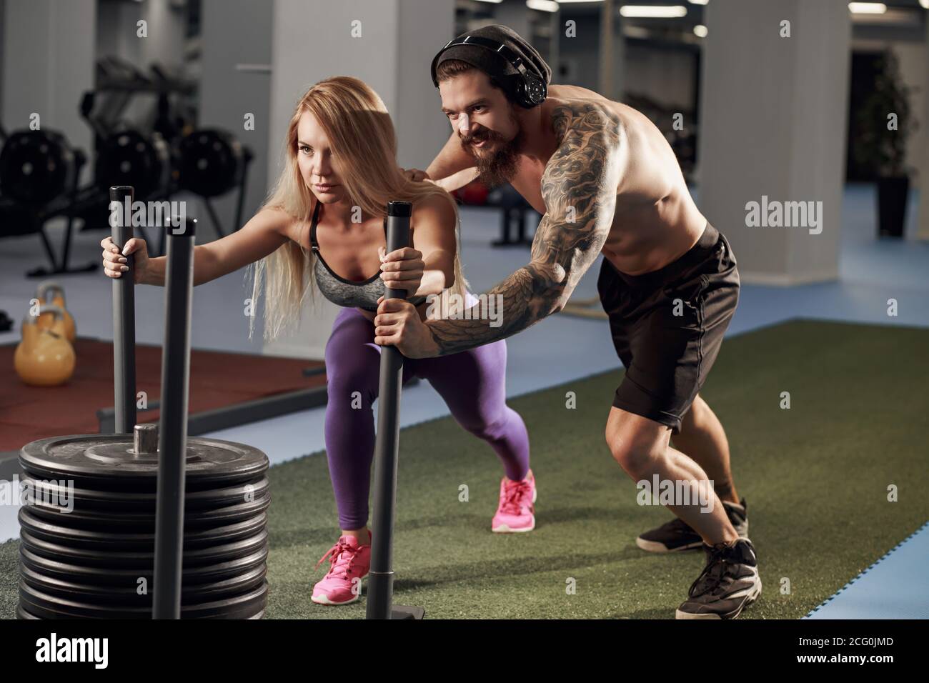 Fitness sled pull with female standing on sled. Two women doing intense ...