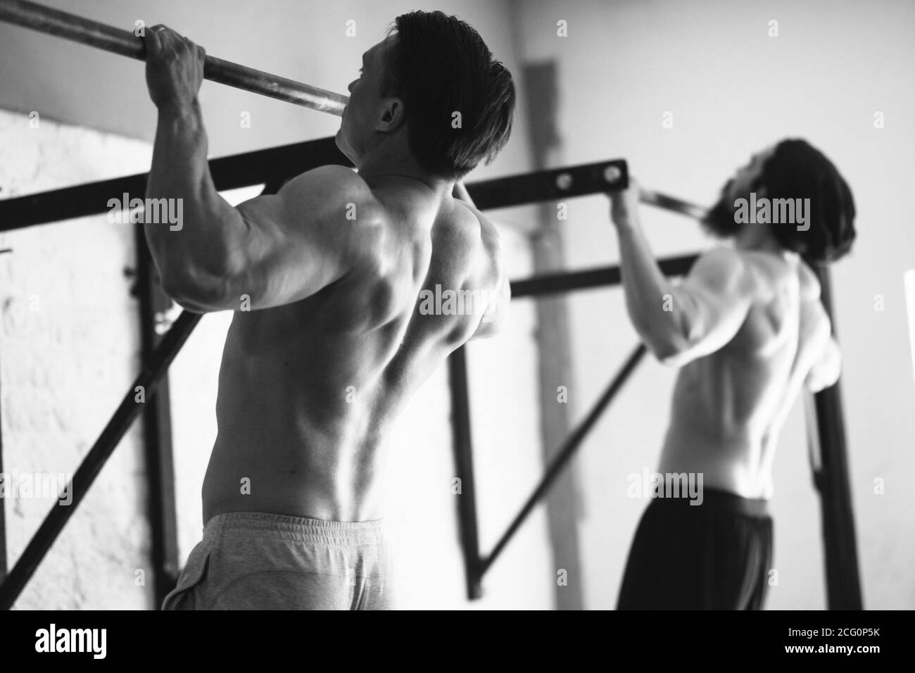 two attractive young male adults doing pull ups on bar in cross fit ...