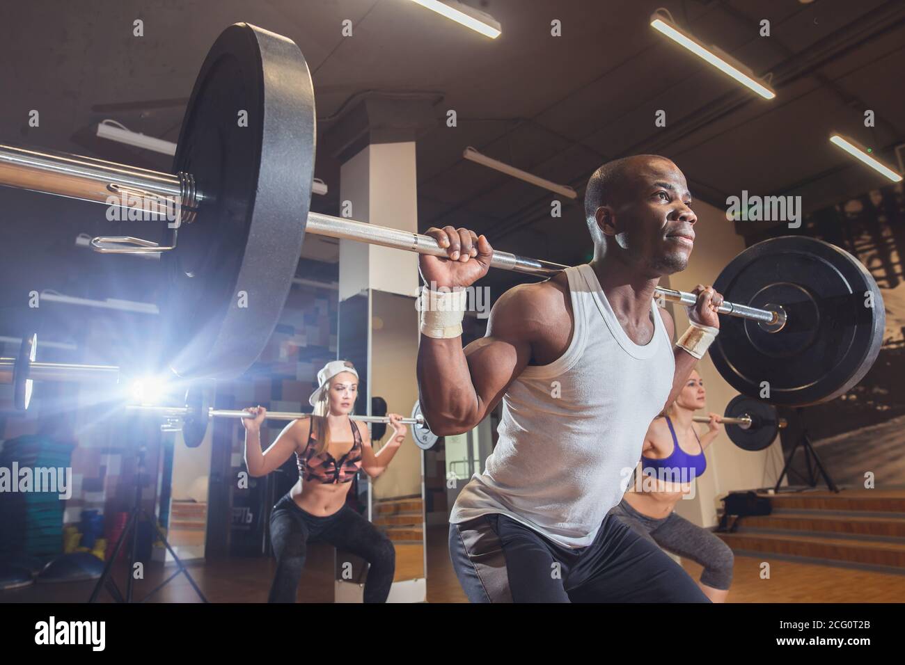 group of young athletes with African trainer doing squats with a ...