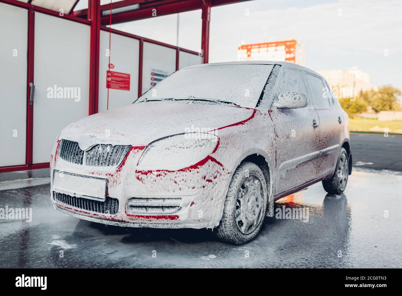 Carwash. Red auto covered with soap foam soaking outdoors. Cleaning ...