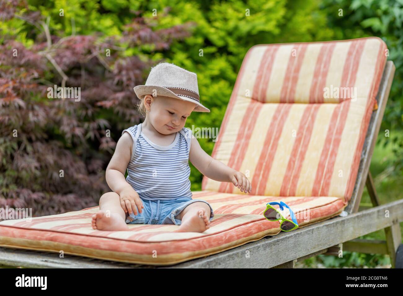 Baby boy is throwing away sunglasses sitting on the deck chair in the ...