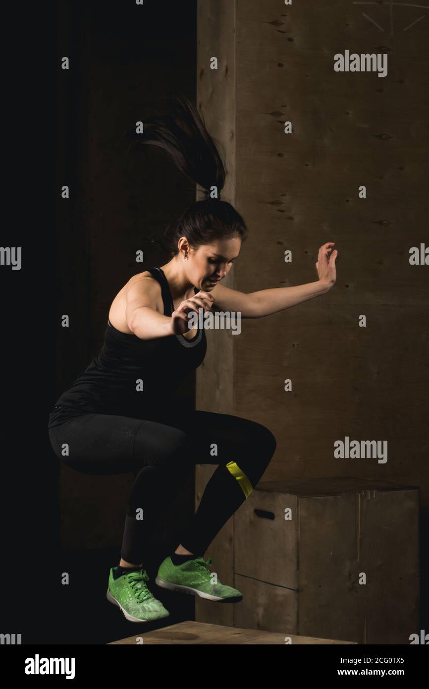 Fit young woman box jumping at a crossfit gym. Female athlete is ...